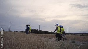 Side view group engineers in wind power plant walking together at sunset for maintenance windmill wear safety clothes and equipped with working tools. Professional technicians men in charge of repair.