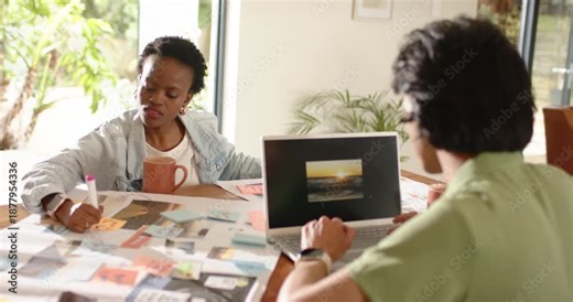 Diverse coworkers scrolling laptop then writing sticky notes refining ideas in sunlit workspace