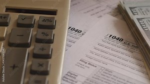 Close-up calculator calculating income expenses, tax form 1040 and US dollar cash nearby