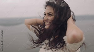 Young and beautiful bride stand on the slope of the mountain near sea. Windy weather. Hair shaking in the wind. Wedding day. Slow motion