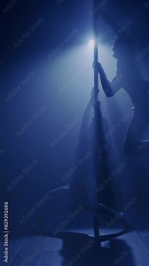 Vertical full shot with slowmo of sensual couple pole dancing under blue projector light in very dark studio