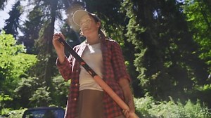 Woman chopping firewood with ax. Female chopping logs on the forest with a huge ax. Young girl chopped wood at summer. . stack of folded chopped wood lies in the summer forest