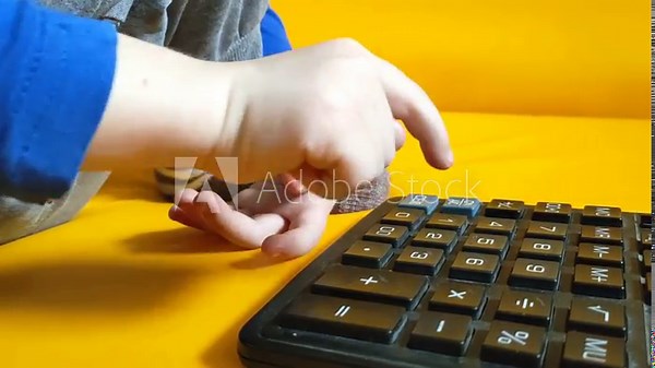 Child hands with calculator counting during school homework. Kid fingers press buttons and calculate studying math at home. A small child counts on a calculator on a yellow background