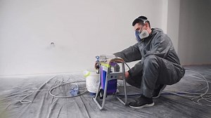 Male builder painter setting up machine for airless wall spray painting. Finishing inside buildings