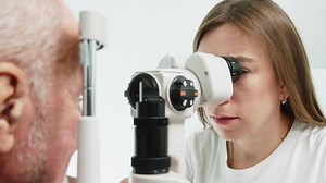 Optician doctor working with the refractometer machine. Eye exam for old man. Female ophthalmology specialist doing eye checkup. Ophthalmologist check eyesight of senior man with modern equipment.