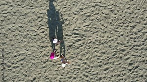 Three children in baseball caps cast long shadows on a sandy beach, drone footage