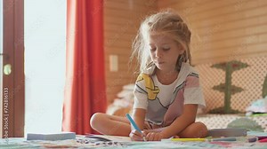 Cute girl drawing sitting lotus position. Adorable preschool girl in casual clothes sitting on bed and drawing in book with felt-tip pens while studying at home