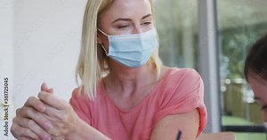 Mother and daughter wearing face masks sanitizing their hands at home