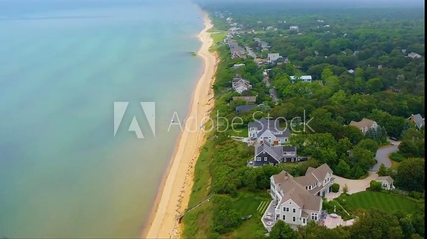 High aerial view of Cape Cod shoreline lined with beach houses, beneath low gray clouds and drifting mist, creating a dramatic seascape where coastal architecture and rugged nature meet at once.