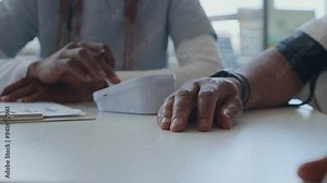 Close up shot of hands of unrecognisable doctor adding medical paper to clipboard and using monitor while measuring patients blood pressure in hospital