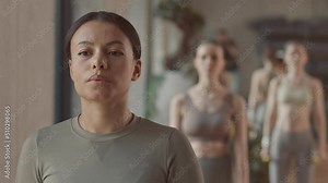 Chest up slowmo of concentrated young Biracial woman doing alternating dumbbell front raise during group pilates training in studio