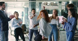Cheerful young woman startup team leader doing funny dance during break in modern office. Company coworkers having fun at work, celebrating success, expressing satisfection.