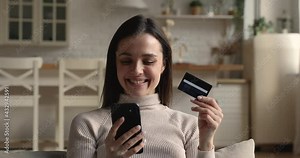 Secure payment through e-bank app, easy instant money transfer, e-commerce happy client concept. Young woman sit on sofa holding smartphone and credit card buying on internet use retail web services