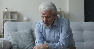 Sad lost grey haired elderly retired man suffering from depression, memory loss, mental Alzheimer disorder, sitting on home couch with pointless stare, looking away, thinking on geriatric disease