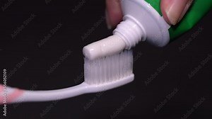 Squeeze a white toothpaste from a tube onto a toothbrush, black background.