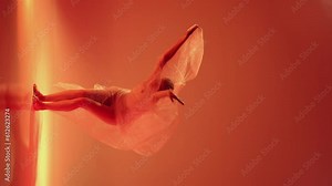 Tender young woman, ballerina dancing with transparent fabric against orange studio background in neon light. Concept of classical art, dance, beauty, creativity, inspiration. Vertical layout