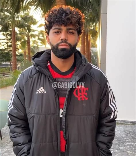 A Man With Curly Hair And Beard Standing In Front Of Palm Trees Wearing