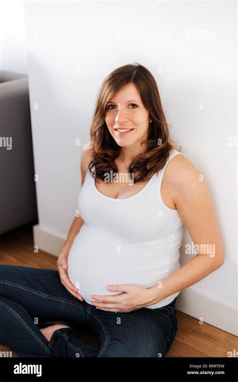 Cheerful Pregnant Woman In White Shirt Sitting On The Floor And Holding