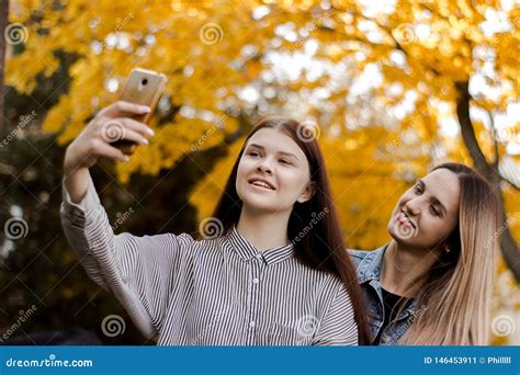 Two Beautiful Smiling Young Girls Taking Selfie On The Phone In The Autumn Park Stock Image
