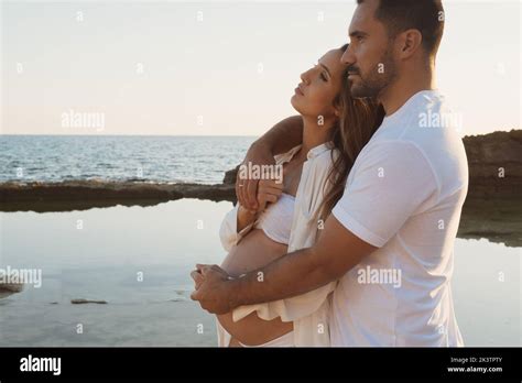Side View Of Man Embracing Pregnant Woman While Standing On Coast Near