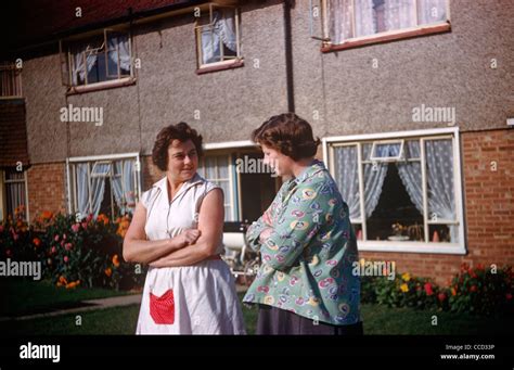 Two Mothers And Neighbours Gossip With Arms Folded Outside Their Houses On An Essex Estate In