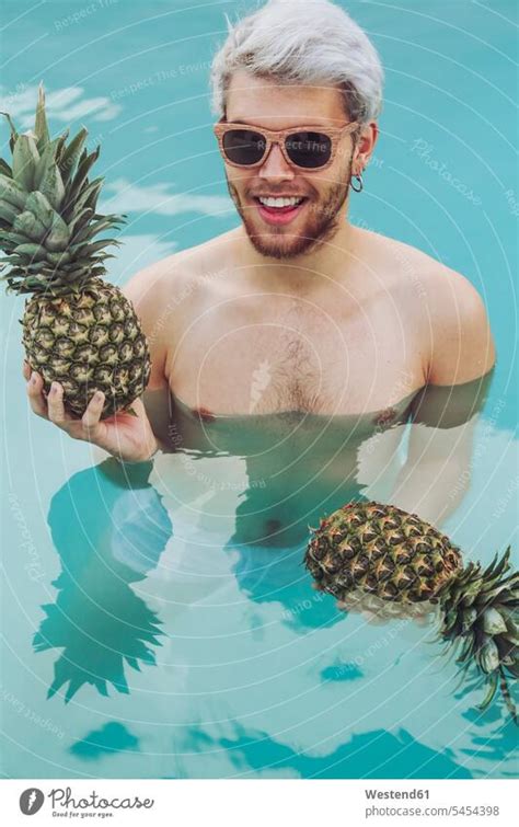 Lächelnder junger Mann hält Ananas im Schwimmbad ein lizenzfreies