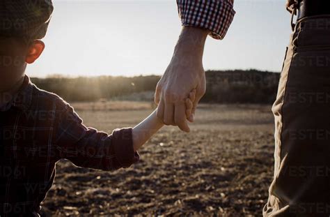 Cropped Image Of Father And Son Holding Hands While Standing On Field
