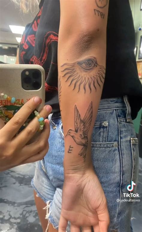 A Person With A Bird Tattoo On Their Arm Holding A Cell Phone And
