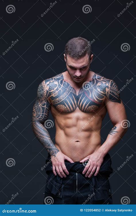 The Man With A Muscular Naked Torso With Tattoos On The Dark Background