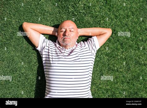 Retired Man Lying On His Back On Grass With Hands On Head With Grass