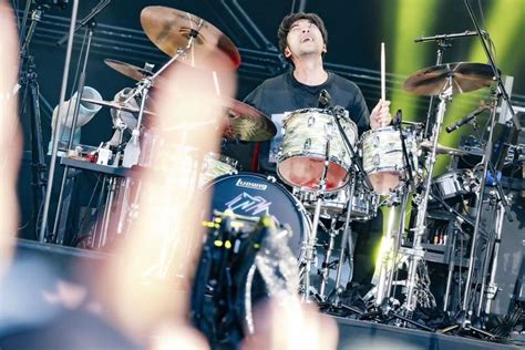A Man Is Playing Drums On Stage With His Hands Up In The Air As He Sings