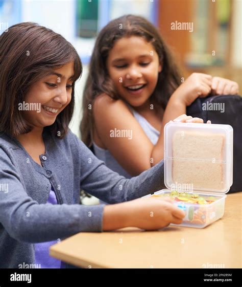 Opening Her Lunch In The Cafeteria Two Young School Girls Sitting In The Cafeteria During