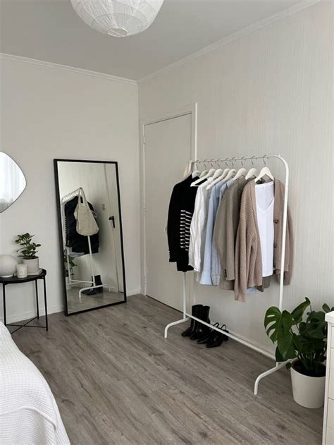 A Bedroom With White Walls And Wooden Flooring Has Clothes On Hangers