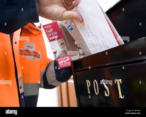 A Royal Mail Postman Delivers Letters Through A Door On His Round In