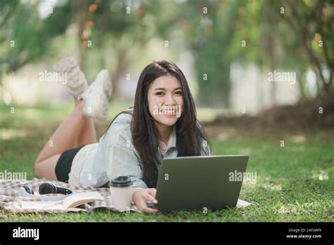 Asian Woman Lying On Picnic Blanket And Lawn At Park Working On Laptop Asian Female Using