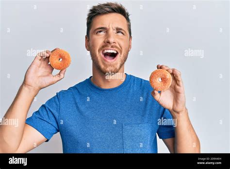 Handsome Caucasian Man Eating Donuts Angry And Mad Screaming Frustrated And Furious Shouting