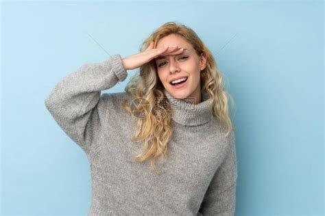 穿着单身蓝背景的毛衣的年轻金发女青年用手向远方望去高清图片下载 正版图片504431559 摄图网
