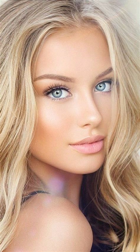 A Beautiful Blond Woman With Blue Eyes And Long Wavy Hair Is Posing For