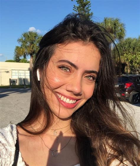 A Woman With Long Brown Hair Smiling At The Camera And Wearing Ear Buds