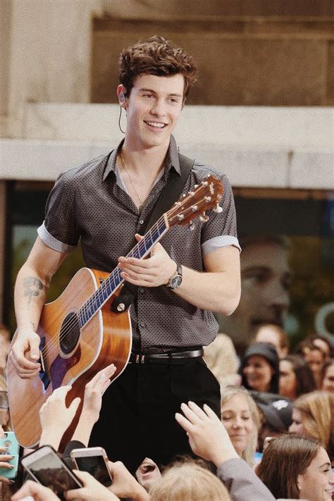 A Man Holding A Guitar While Standing In Front Of A Crowd