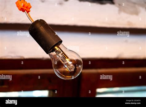 Closeup Of A Light Bulb Hanging From Wires On A Wall With A Blurry