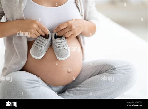 Unrecognizable Pregnant Woman Holding Baby Shoes On Her Big Belly Stock