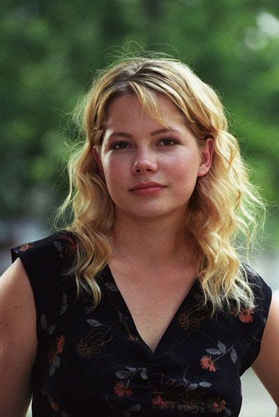A Woman With Blonde Hair Wearing A Black Top And Looking At The Camera While Standing In Front