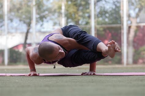 Mujer cabeza rapada tatuada en pose de yoga de ocho ángulos