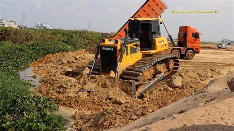 A Bulldozer Digging Dirt In Front Of A Dump Truck