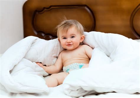Lindo bebé sentado en una cama envuelto en una manta blanca el bebé