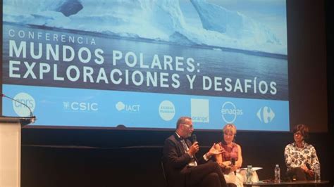 Two People Sitting On Stage In Front Of A Screen With An Iceberg Behind