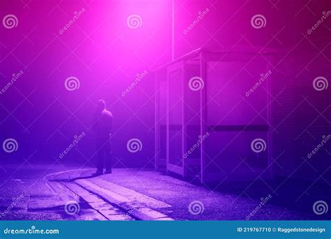 A Mysterious Hooded Man Standing Next To A Bus Stop Under A Street