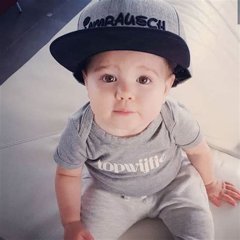 A Baby Wearing A Baseball Cap Sitting On Top Of A White Couch With His