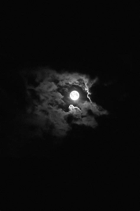 The Full Moon Shines Brightly In The Dark Night Sky With Clouds And